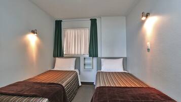 Quarto de hotel com duas camas de solteiro, uma janela com cortinas e luminárias fixadas na parede.