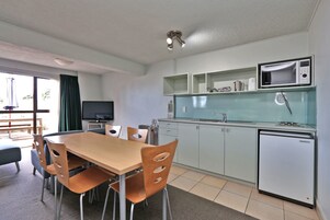 Cozinha compacta com micro-ondas, pia e pequena geladeira. Possui um espaço de refeições com mesa e cadeiras.