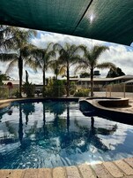 Piscina com águas cristalinas, cercada por palmeiras e uma área delimitada por cerca.
