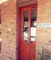 Uma área de recepção com porta de madeira, um timbre e um aviso com o horário de funcionamento.
