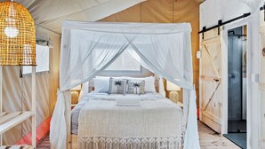 Quarto tipo tenda com cama de dossel, luminária pendente e porta de madeira.