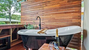 Um banheiro externo moderno com uma banheira independente, um deck de madeira e vista para uma casa e árvores.