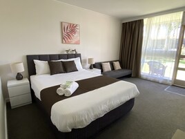 Quarto de hotel com uma cama grande, um sofá, uma mesa de cabeceira com abajur, uma obra de arte na parede e vista para o exterior pela janela.