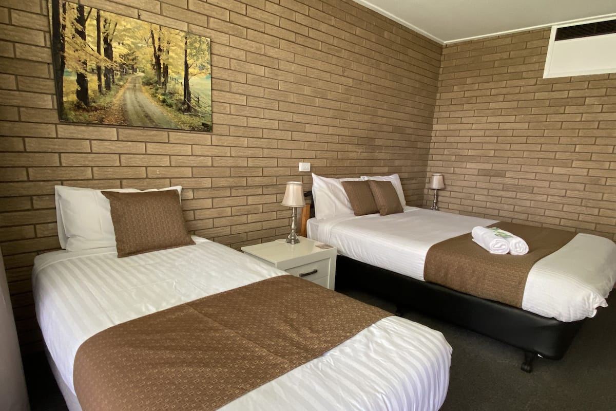 Quarto de hotel com duas camas, um quadro de uma floresta na parede e uma parede de tijolos.