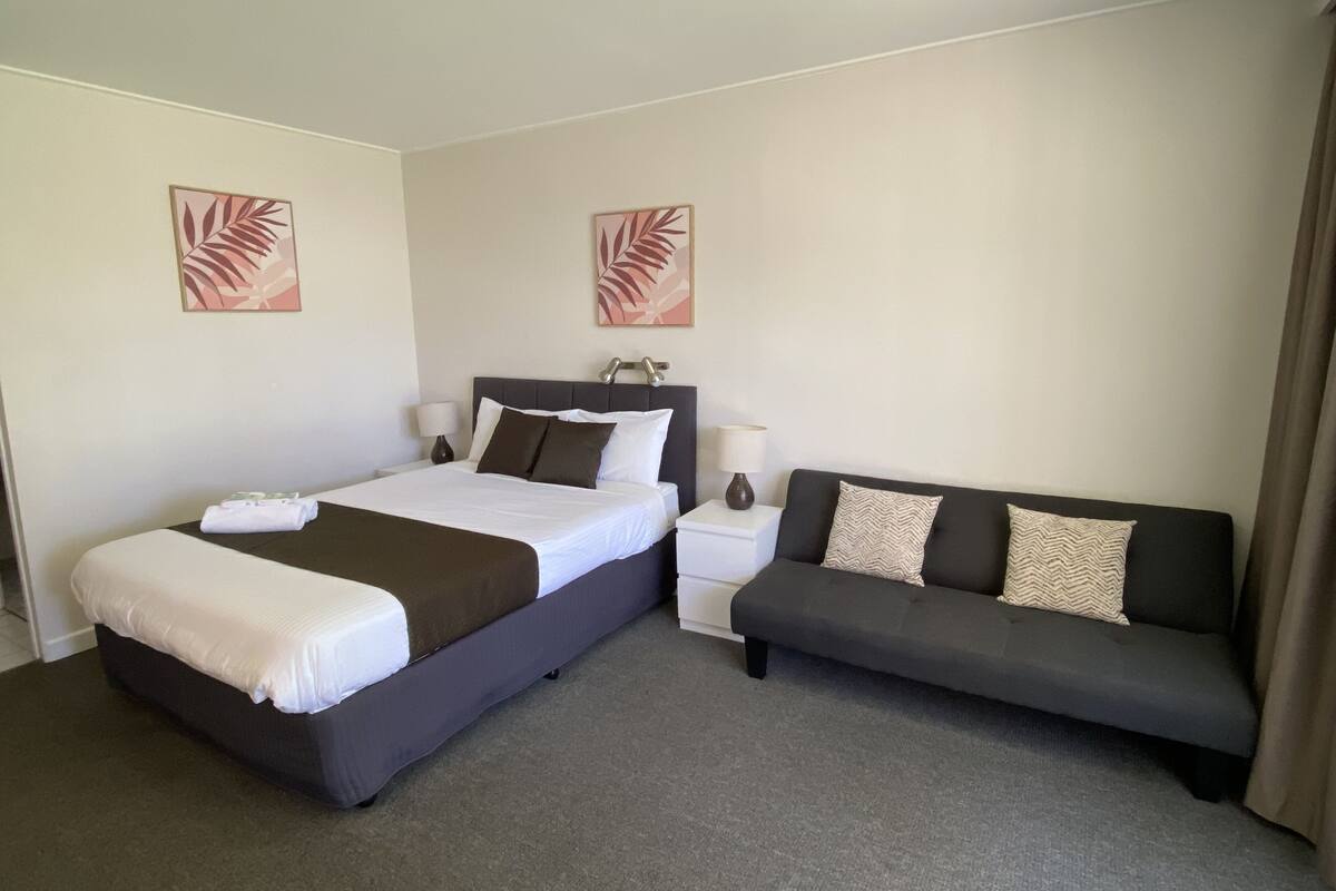 Quarto de hotel com cama, mesas de cabeceira, sofá e duas obras de arte na parede.