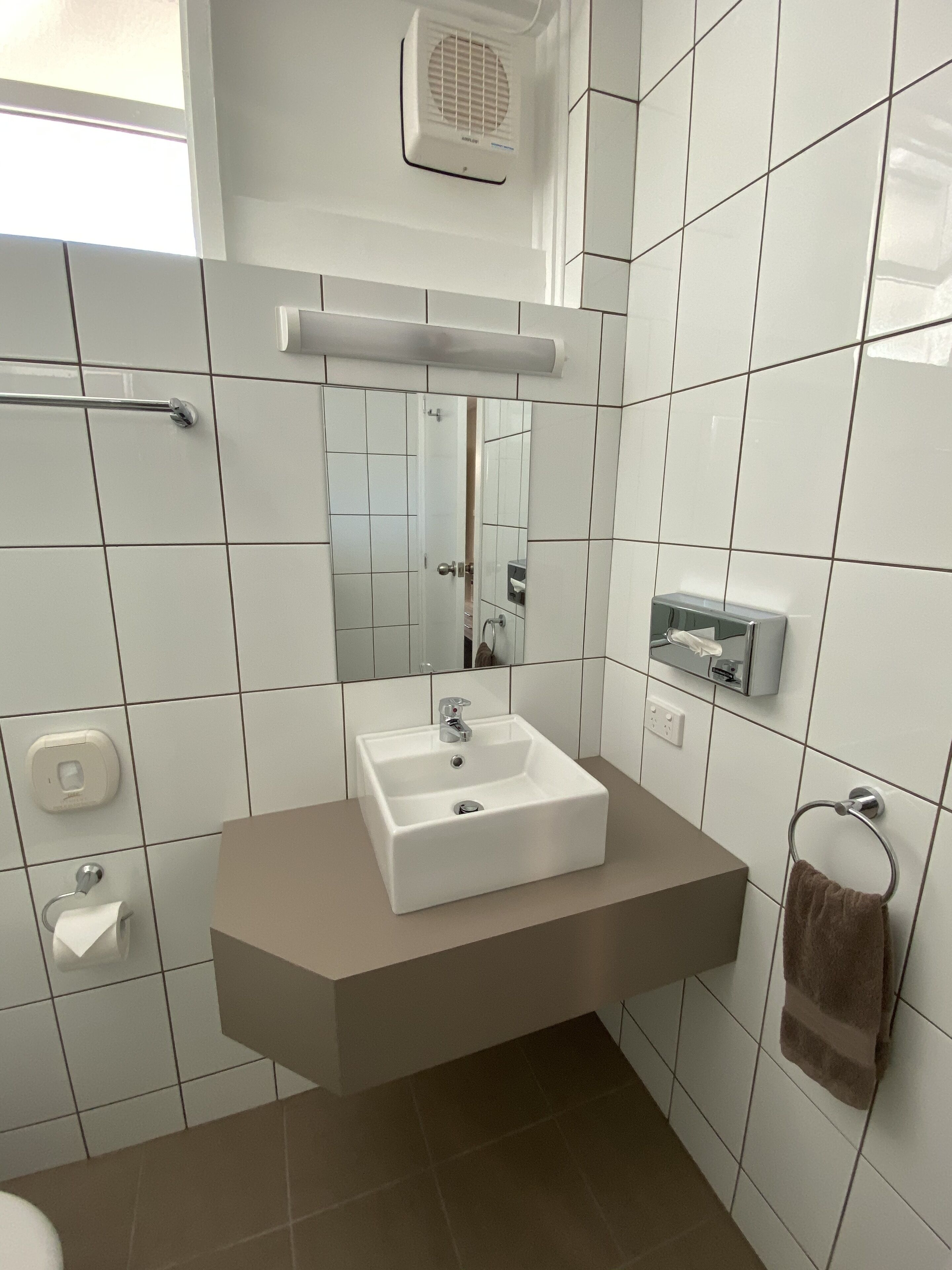 Casa de banho com lavatório branco, espelho, porta-toalhas e secador de mãos.