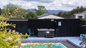 Piscina com hidromassagem e cadeiras, cercada por uma cerca de madeira e vegetação.