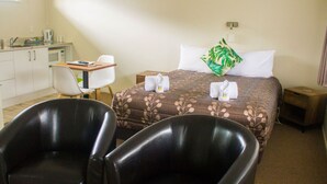 Quarto de hotel com uma cama, duas cadeiras, uma mesa e uma pequena mesa de apoio.