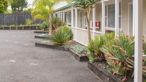 Um edifício com varanda, rodeado por diversas plantas e uma entrada de automóveis em cascalho.
