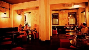 Restaurante com iluminação suave, com cabines e mesas, área de bar e cozinha visível ao fundo.
