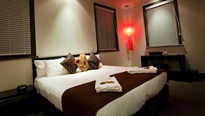 Quarto de hotel com uma cama bem arrumada, uma escrivaninha e uma luminária vermelha na parede.