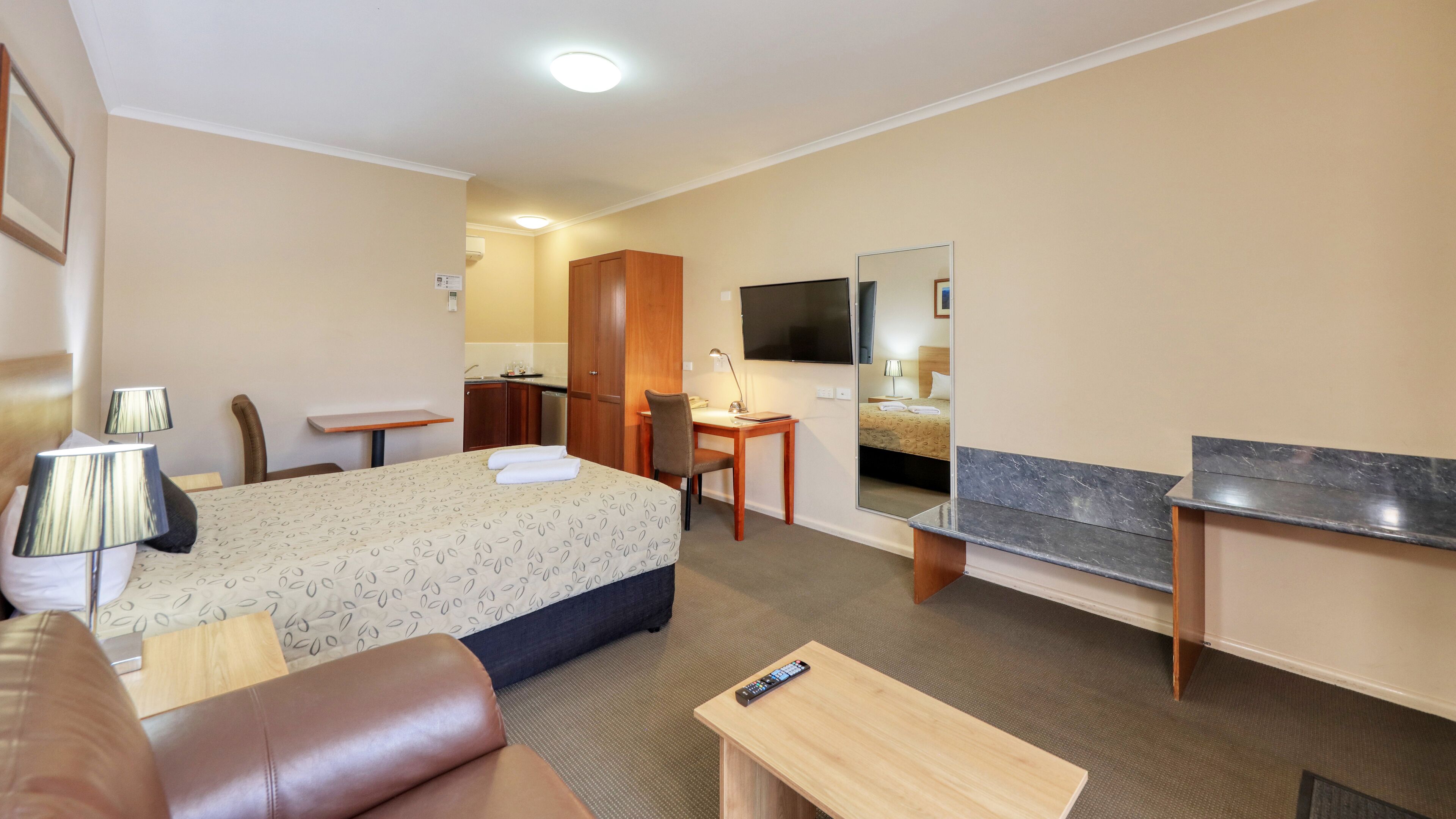Quarto de hotel com cama, escrivaninha, cadeira, sofá, mesa pequena, televisão e espelho.