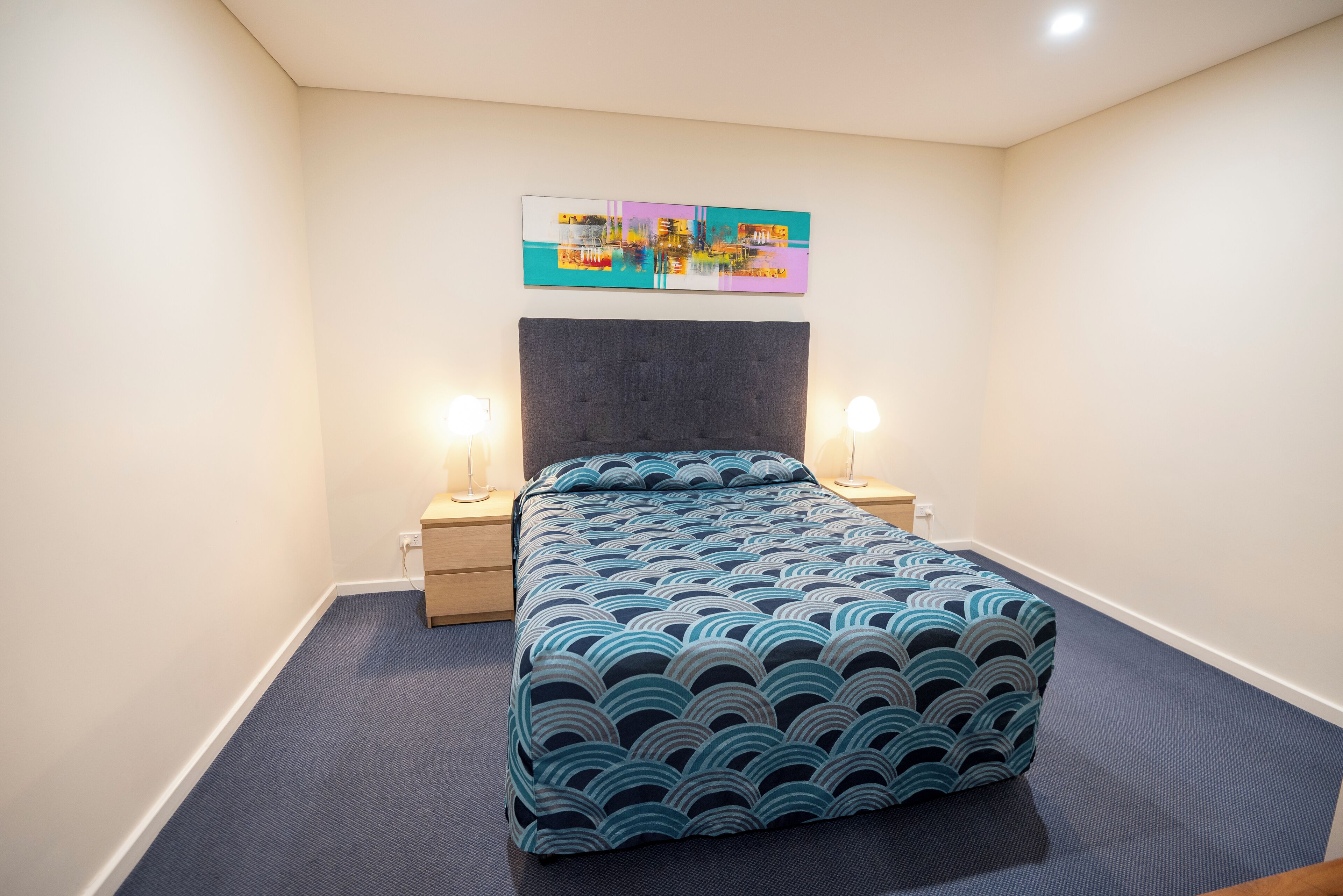 Quarto bem arrumado com uma cama, duas mesas de cabeceira e uma obra de arte na parede.
