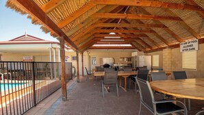 Uma área externa coberta com piscina, mesas e cadeiras.