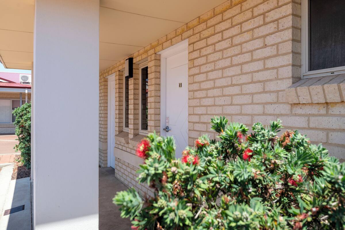 Um edifício com fachada de tijolos, uma porta branca com o número 49 e uma pequena varanda.