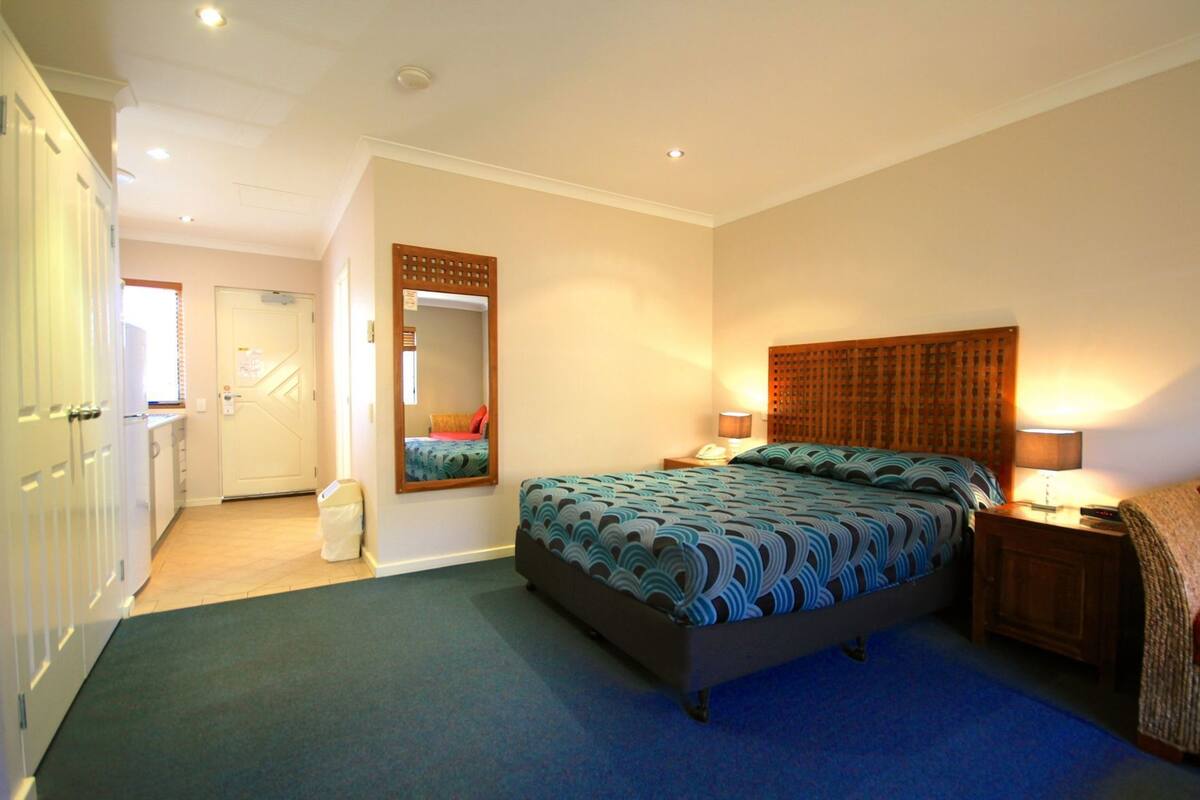 Quarto com cama, mesa de cabeceira, espelho e porta.