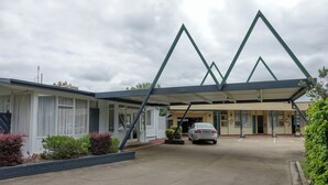 Um motel com estrutura de telhado triangular marcante, área de estacionamento coberta e um carro branco estacionado em frente.