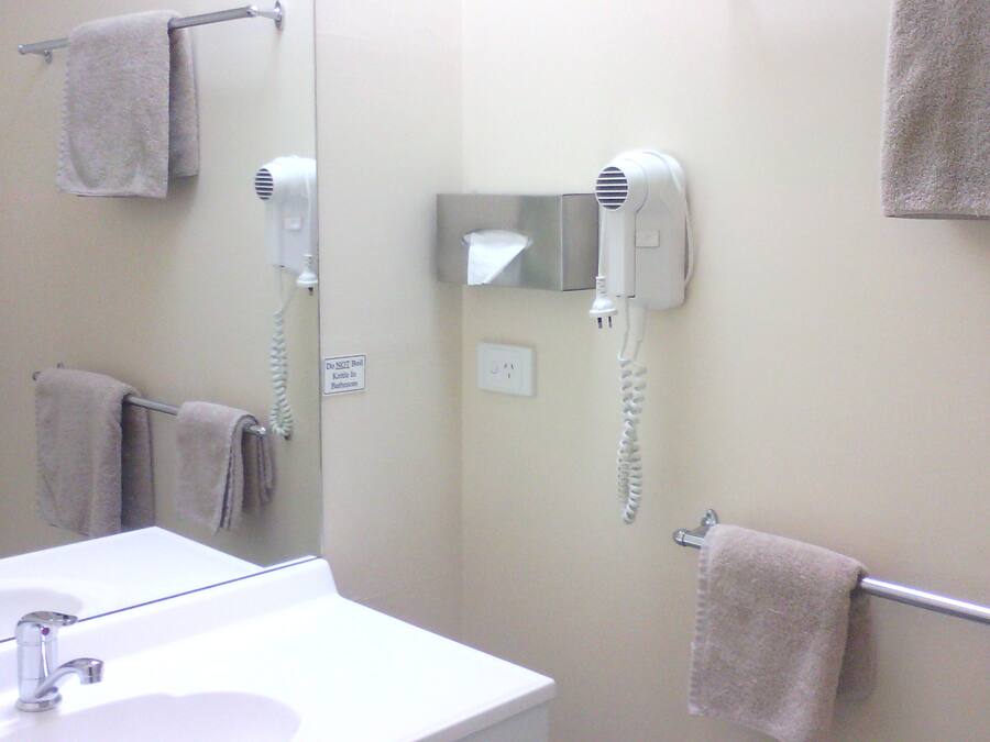 Uma casa de banho com lavatório, porta-toalhas, secador de cabelo e um aviso a proibir chaleiras.