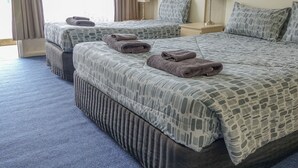 Quarto de hotel com duas camas, cada uma com colcha estampada e almofadas, e um par de toalhas em cada cama.