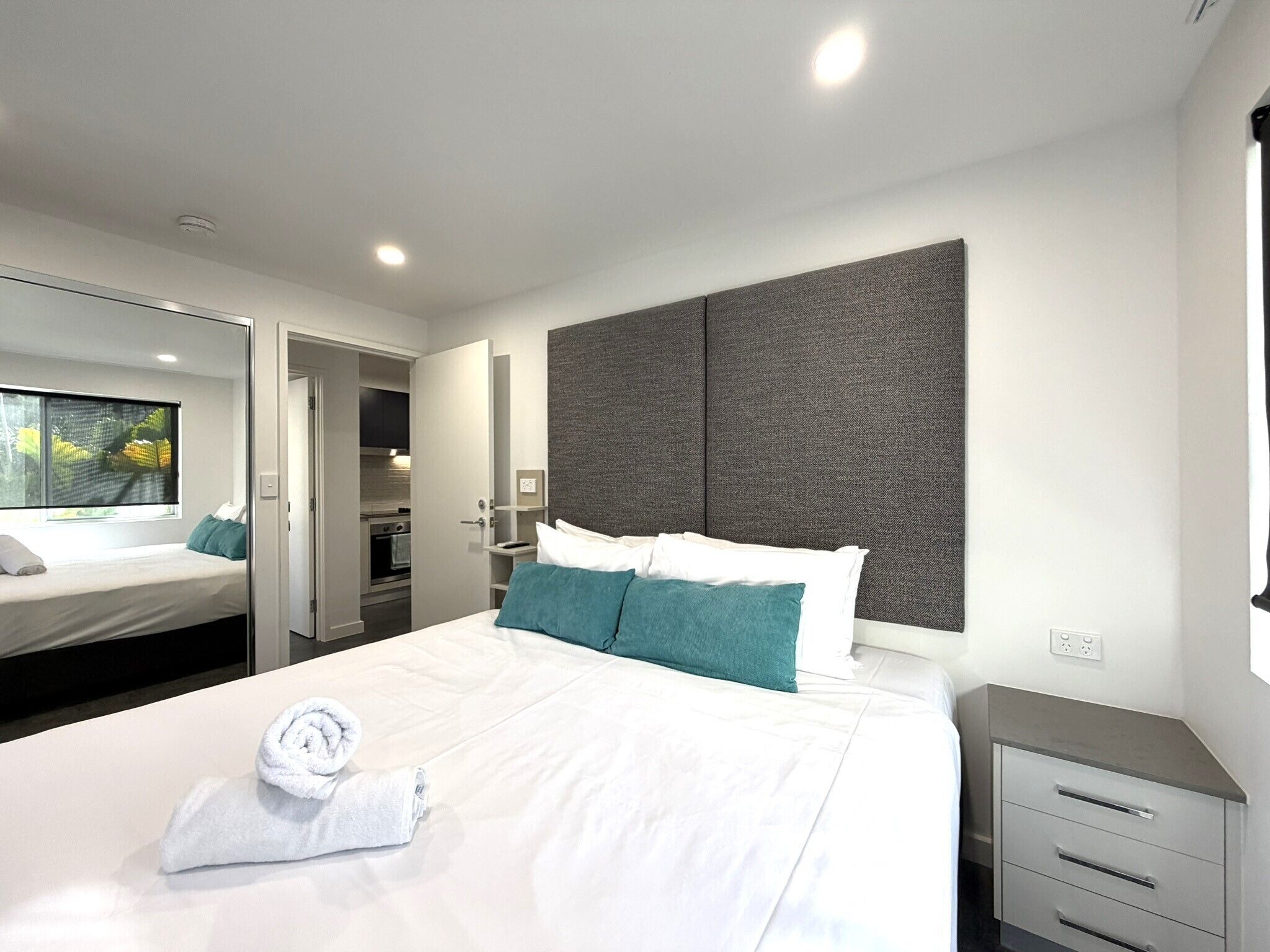 Quarto de hotel moderno com cama grande, closet espaçoso, forno embutido e uma janela ampla com vista para árvores.
