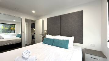 Quarto de hotel moderno com cama grande, closet espaçoso, forno embutido e uma janela ampla com vista para árvores.