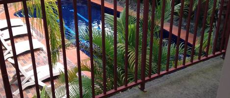Uma área de piscina com guarda-corpo de metal vermelho, rodeada por palmeiras e um caminho de tijolos.