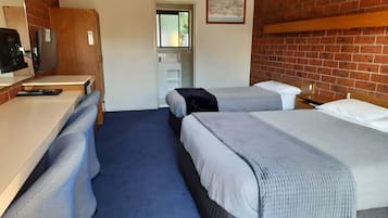 Quarto de hotel com duas camas, uma escrivaninha, uma televisão e uma parede de tijolos.