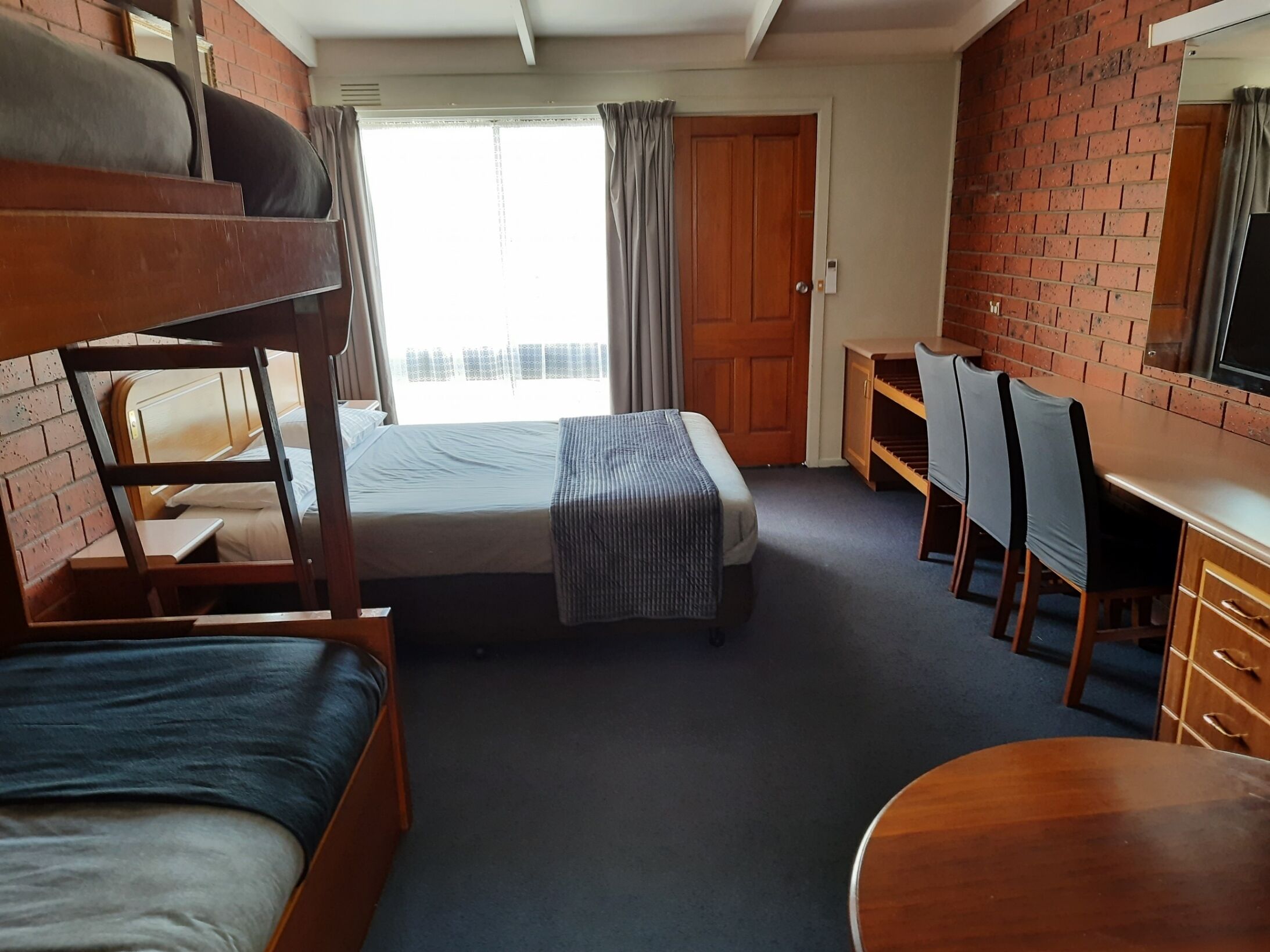 Quarto com beliches, escrivaninha, cadeiras e televisão.