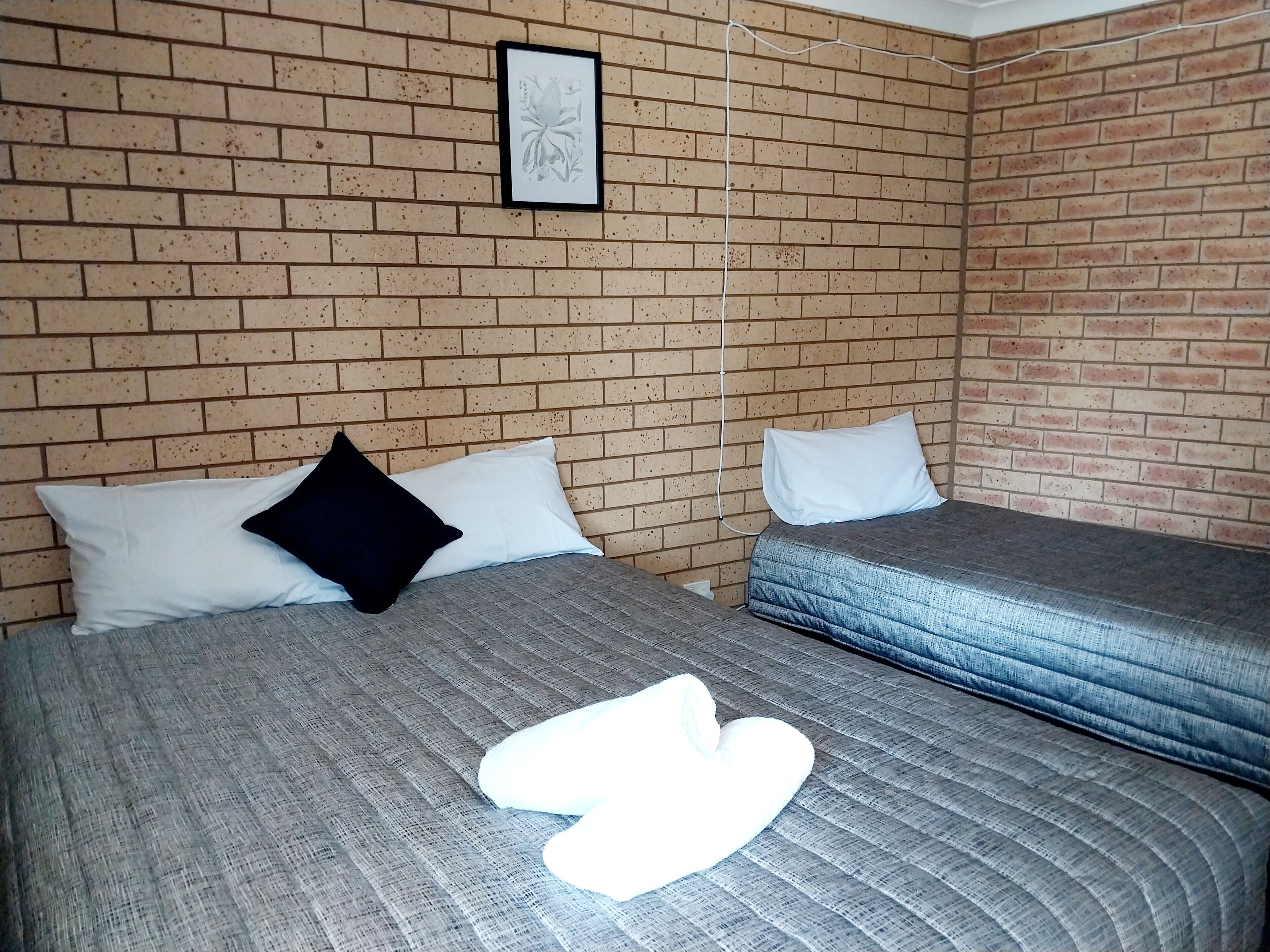 Quarto com parede de tijolos, cama com roupa de cama cinza e travesseiro branco.