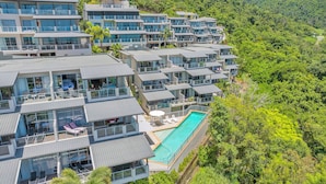 Um resort moderno com vários edifícios de dois andares, uma piscina central e vegetação exuberante ao redor.