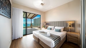 Quarto moderno com uma cama grande, mesa de cabeceira, lumin ária e vista para o oceano através de uma porta de correr.