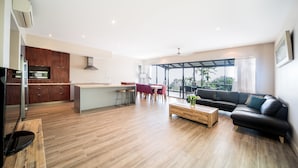 Sala de estar moderna com sofá de couro preto, mesa de centro de madeira e área de jantar com cadeiras vermelhas.