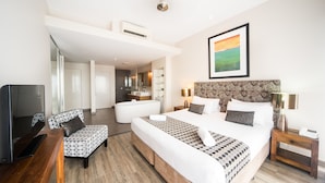 Quarto de hotel moderno com uma cama grande, um sofá, uma TV e uma escrivaninha.