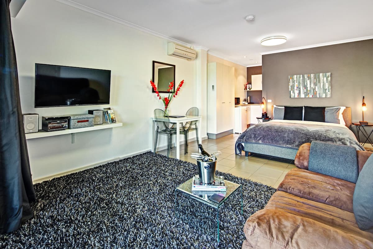Sala moderna com televisão de tela plana, área de jantar com mesa de vidro, sofá e cama em tons de cinza e azul.