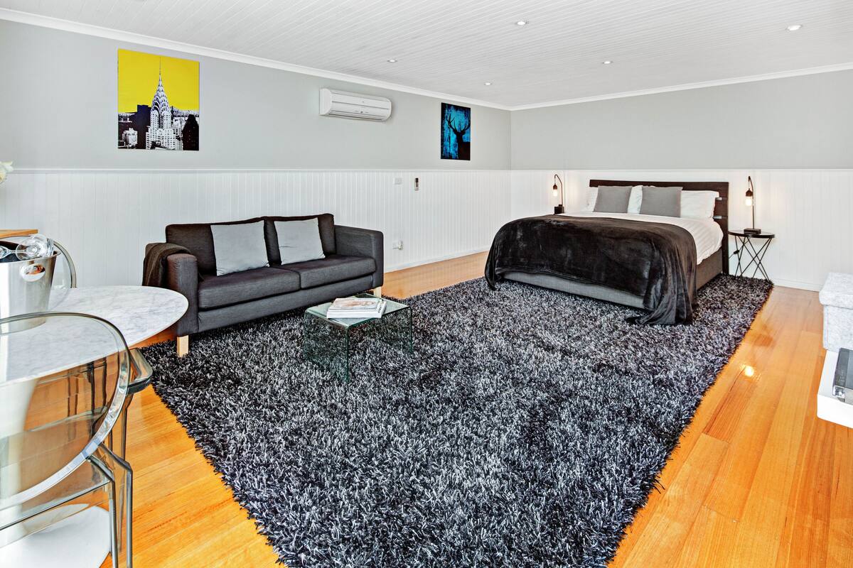 Quarto moderno com cama, sofá, mesa de centro e área de refeições com mesa e cadeiras.