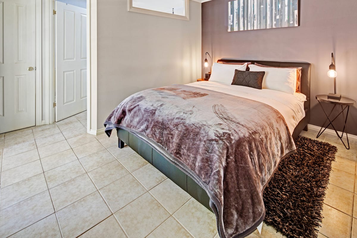 Quarto com cama, mesa de cabeceira, luminária, tapete e porta.