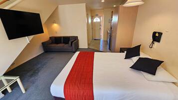 Quarto de hotel com cama, televisão na parede, sofá, telefone e placa de saída.