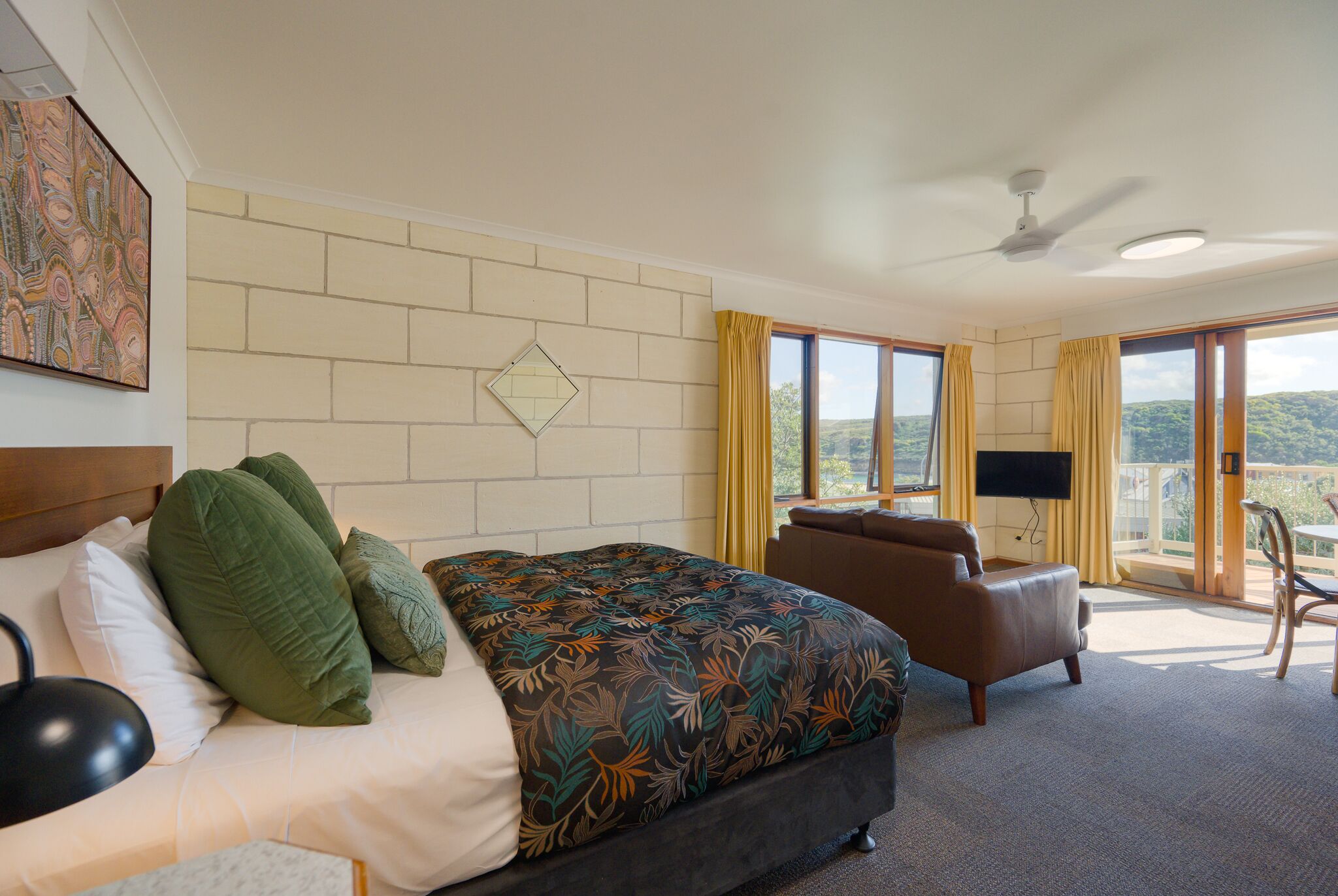 Quarto de hotel com cama, poltrona, televisão e varanda com vista.