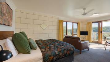 Quarto de hotel com cama, poltrona, televisão e varanda com vista.