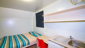 Quarto pequeno e compacto com uma cama, uma cadeira vermelha, uma pia e uma pequena cozinha.