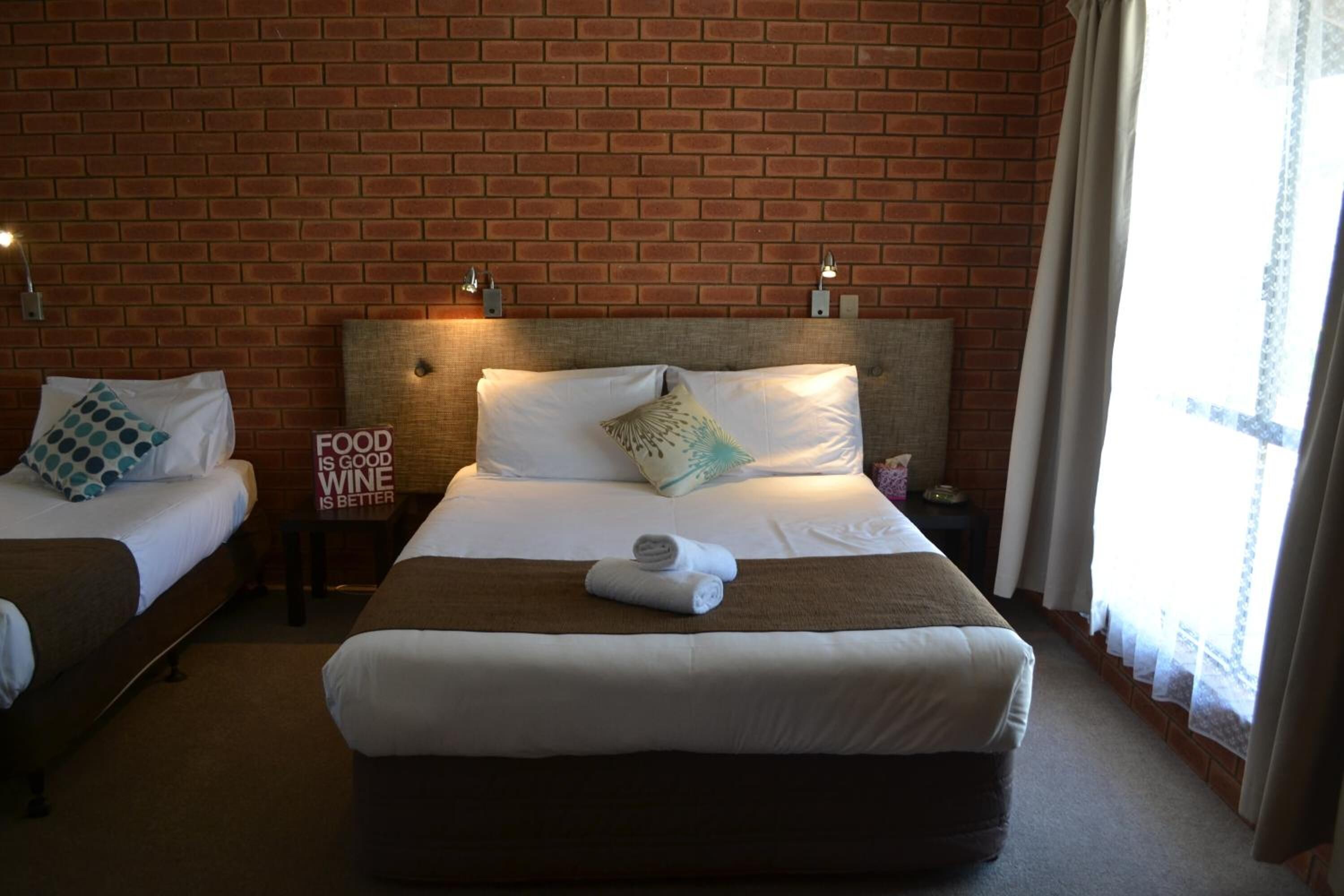 Quarto de hotel com duas camas, uma parede de tijolos e uma janela com cortinas.