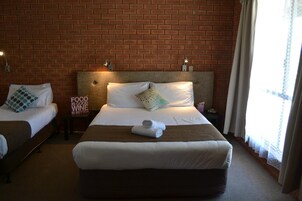 Quarto de hotel com duas camas, uma parede de tijolos e uma janela com cortinas.