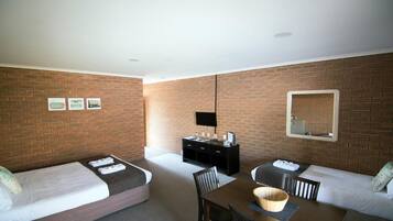 Quarto de hotel com duas camas de solteiro, uma pequena escrivaninha com cadeira, televisão e espelho numa parede de tijolos.