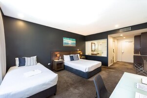 Quarto de hotel com duas camas, uma escrivaninha e um espelho.