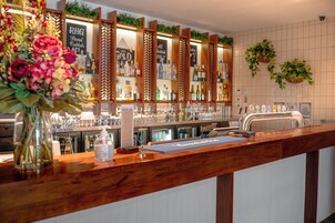Uma área de bar com balcão de madeira, diversas garrafas, copos e um quadro de cardápio.