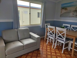 Uma sala de estar com um sofá bege, uma mesa de jantar de madeira com cadeiras brancas e uma janela com cortinas.