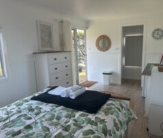 Quarto com cama, penteadeira, espelho e porta que dá para uma varanda.