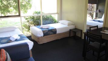 Quarto de hotel com duas camas, uma mesinha, uma cadeira e vista para o exterior.