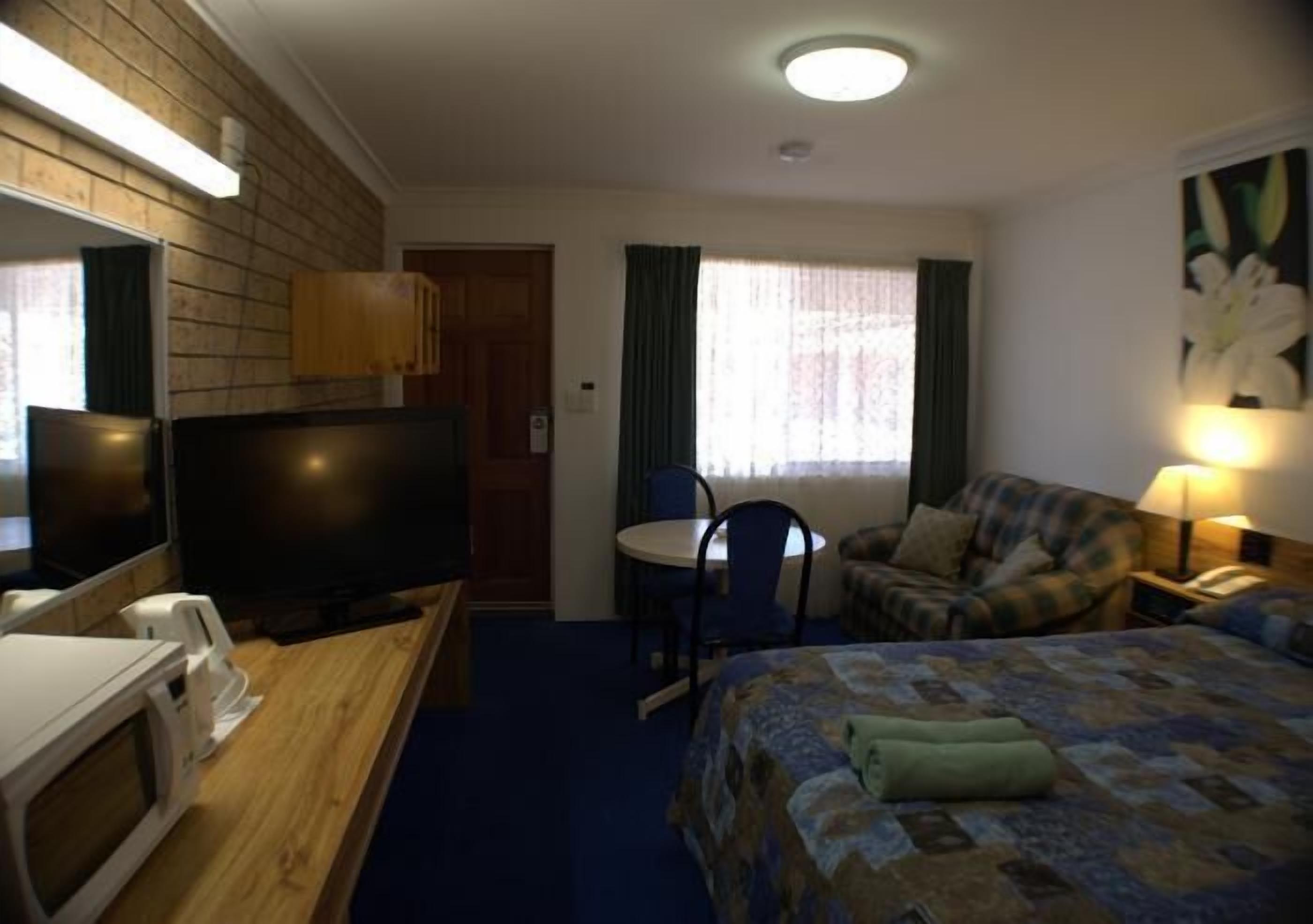 Quarto de hotel com uma cama, televisão, escrivaninha com micro-ondas, cadeira, mesa e sofá.