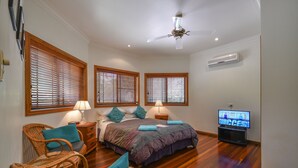 Quarto com cama, duas mesas de cabeceira, televisão e ventilador de teto.
